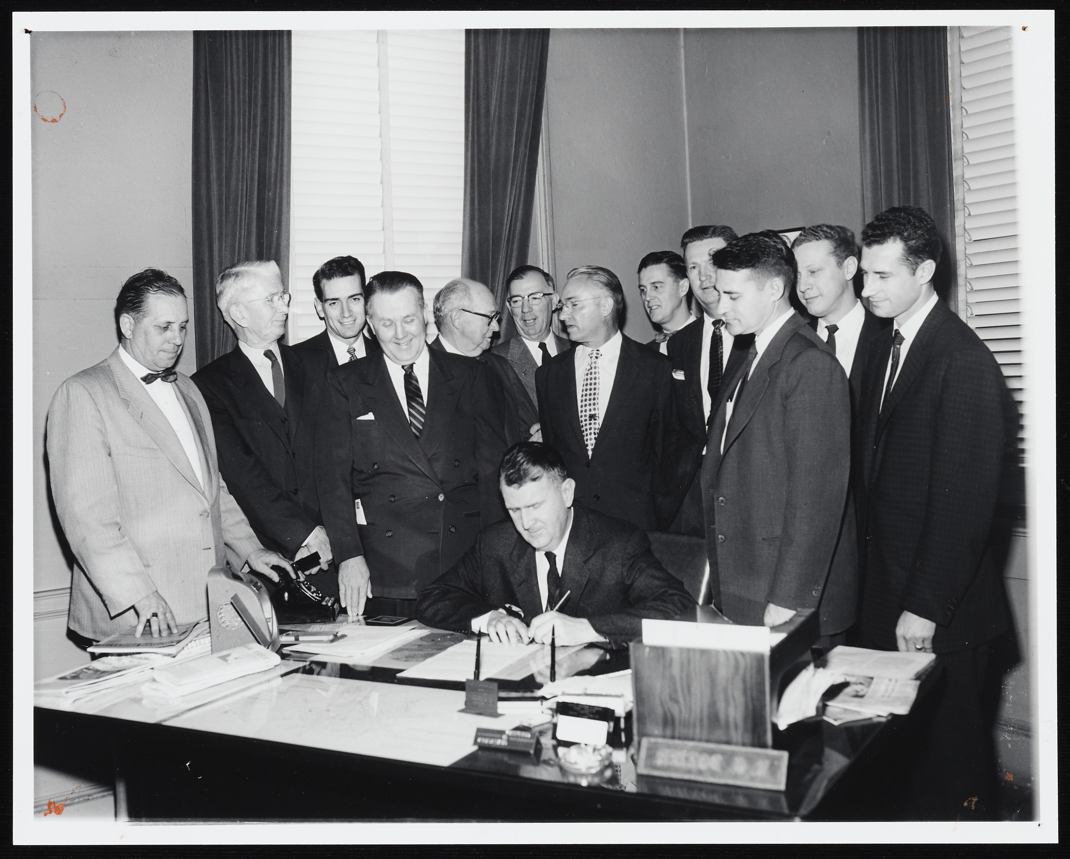 Crowd gathering around a man signing something at a desk, all dressed ...